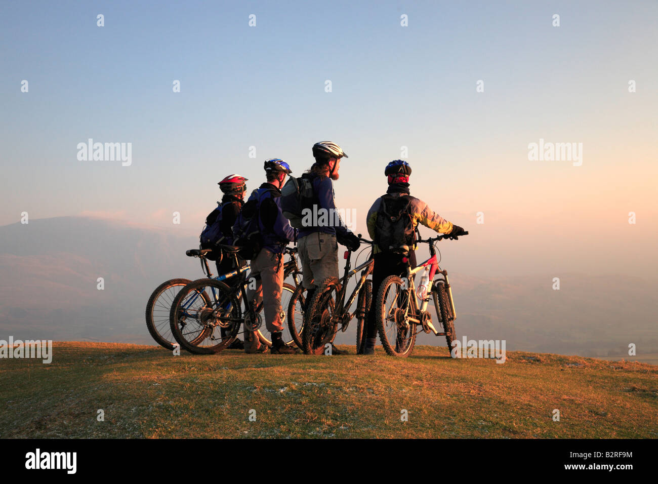 Group of mountain bikers take time to watch the sunset on top of a ...