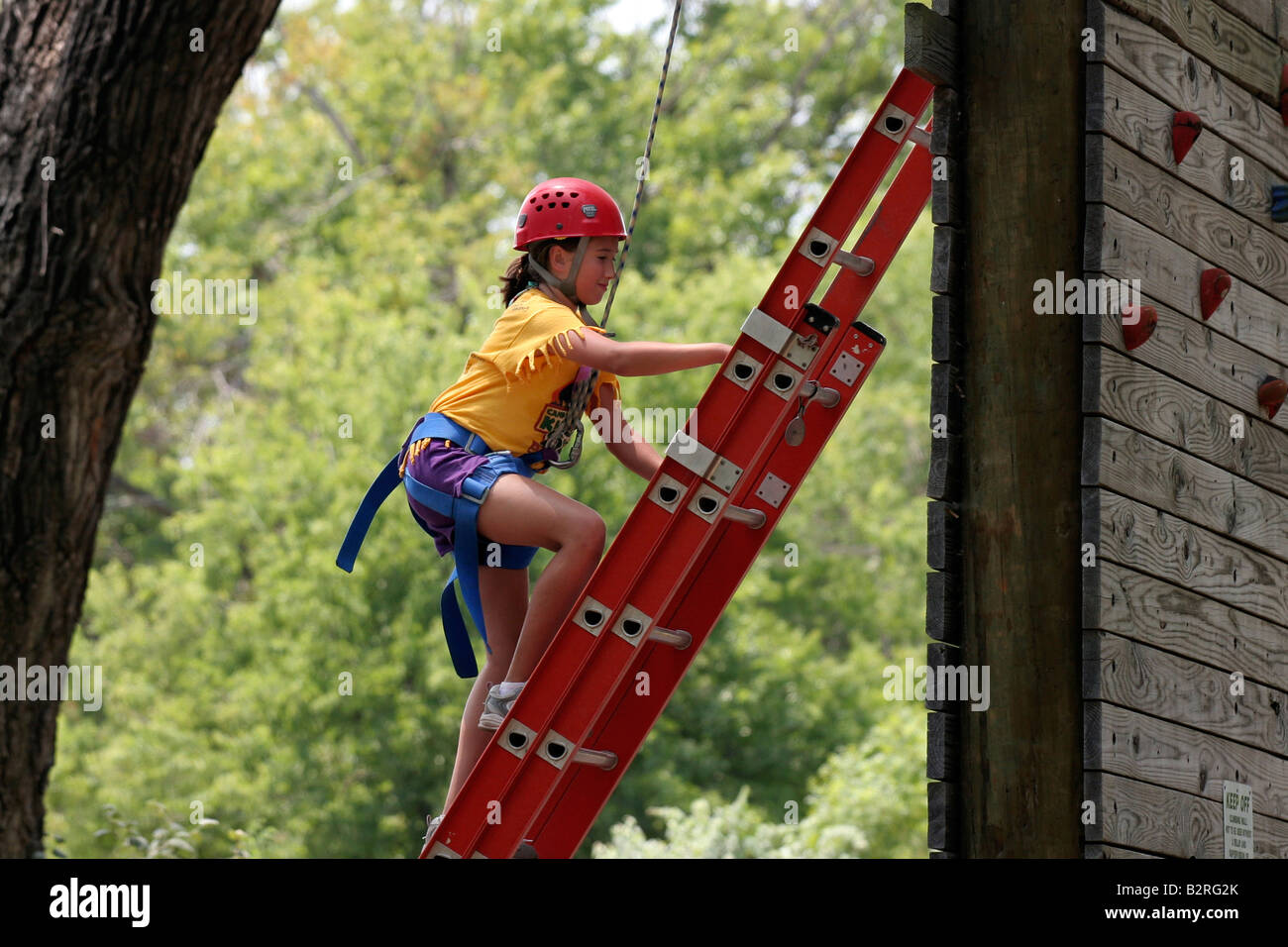 Young girl camper starts to climb up the tall rock wall leading to the ...