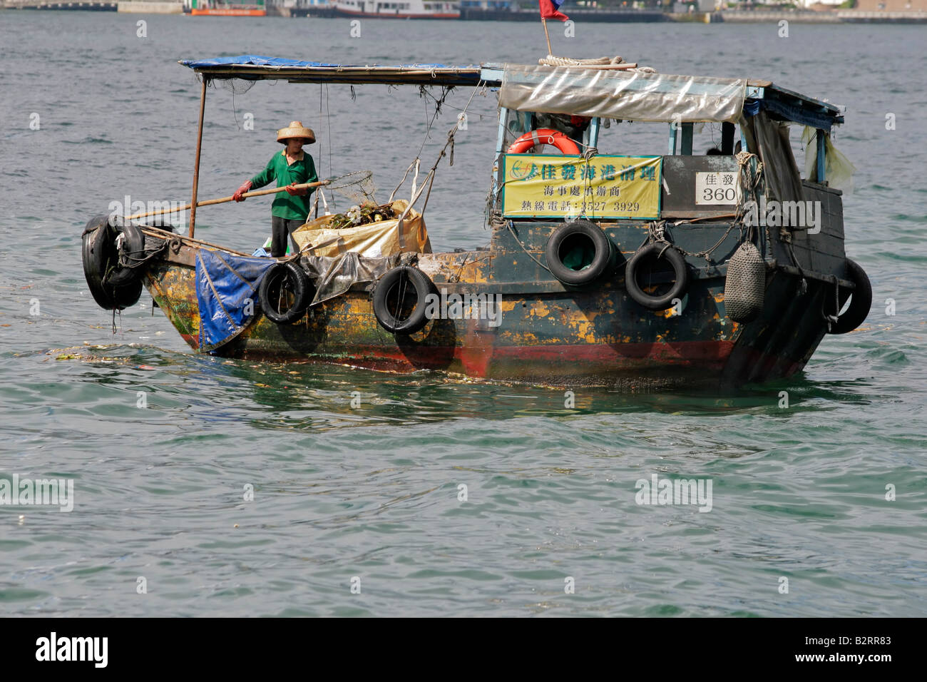 A Chinese worker removing floating garbage from the water in Hong Kong ...