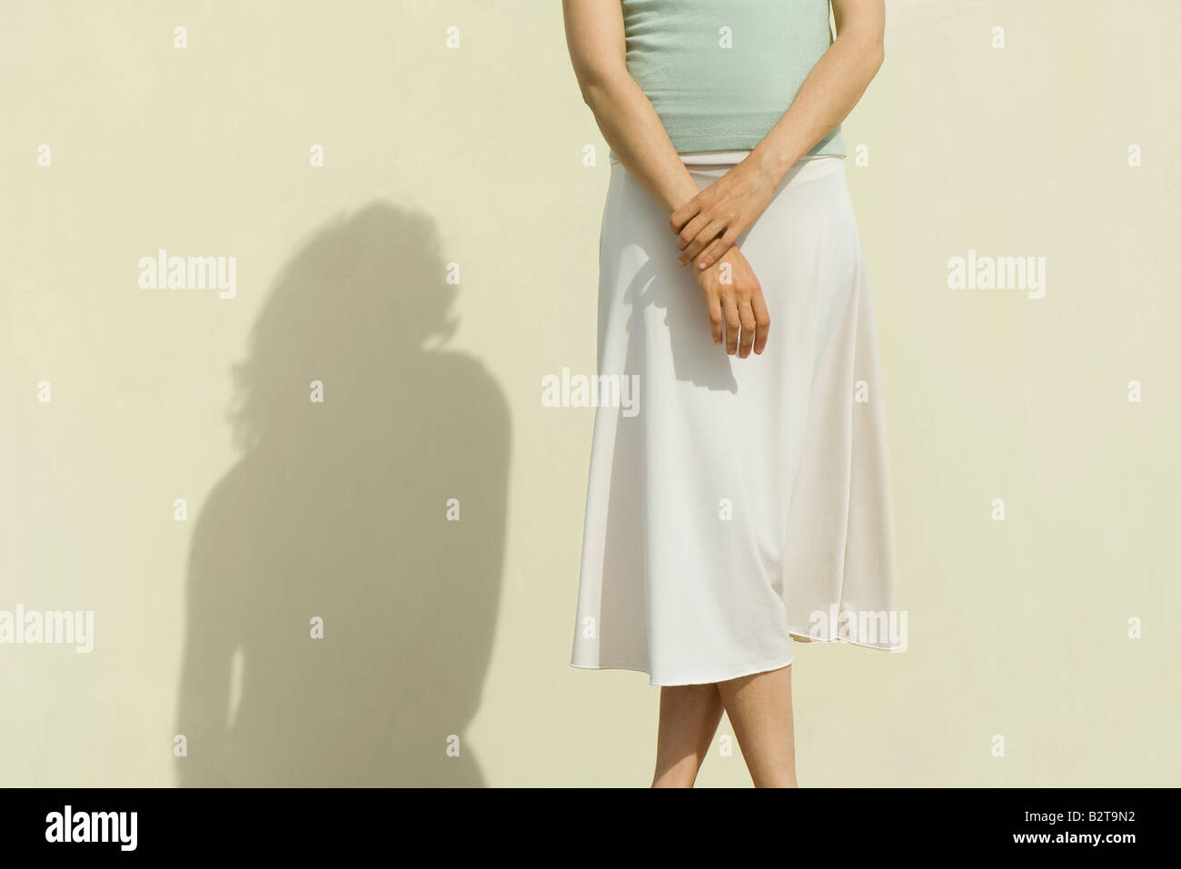 Woman in skirt standing beside shadow, arms folded, cropped view Stock ...