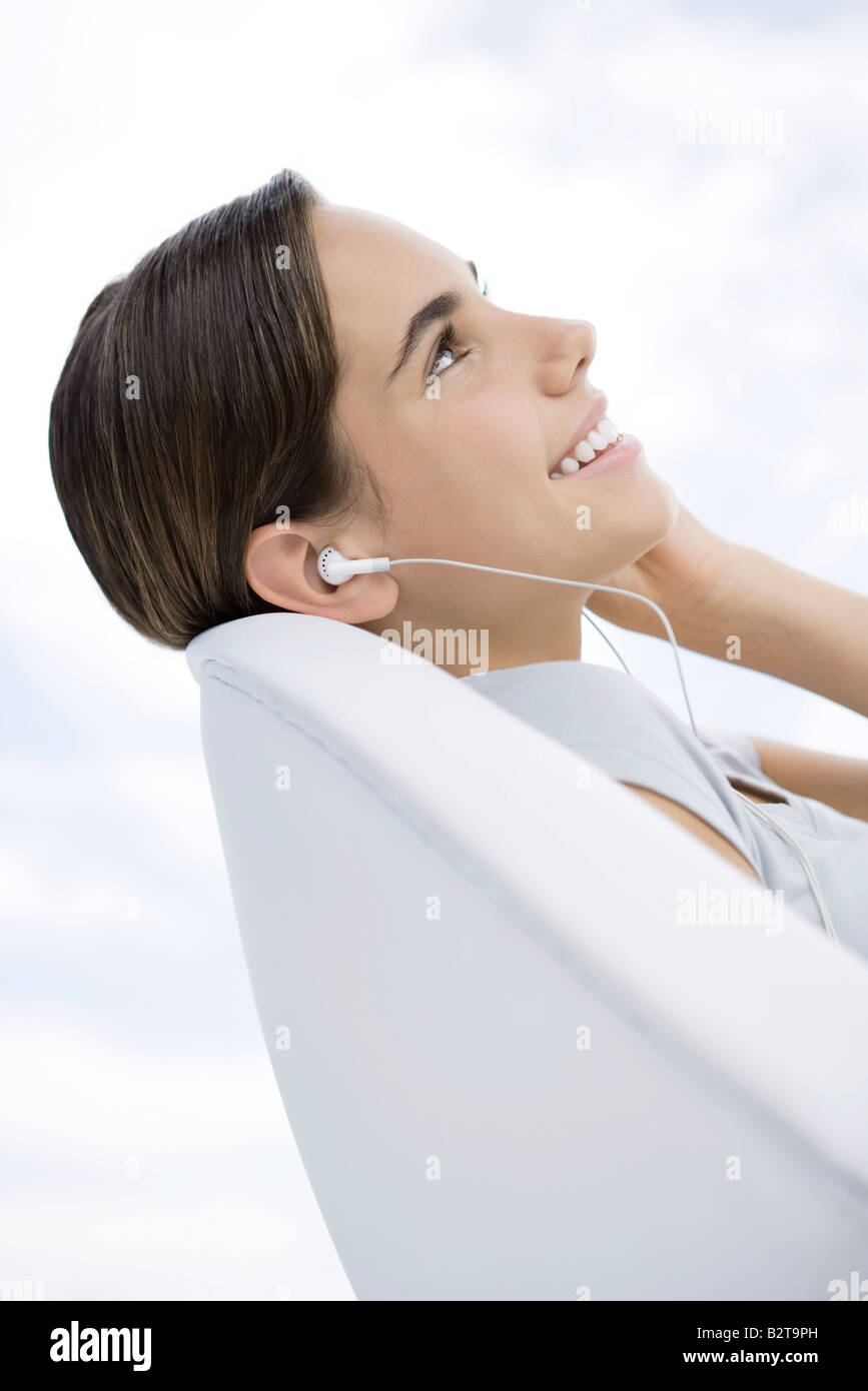 Female leaning back, listening to earphones, side view Stock Photo - Alamy
