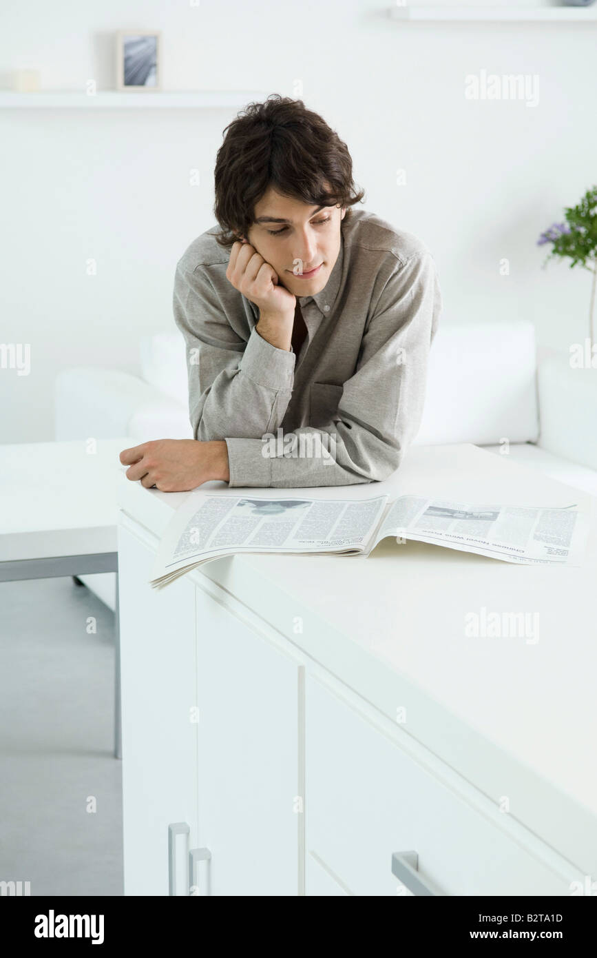 Man leaning against counter on elbows, reading newspaper Stock Photo ...