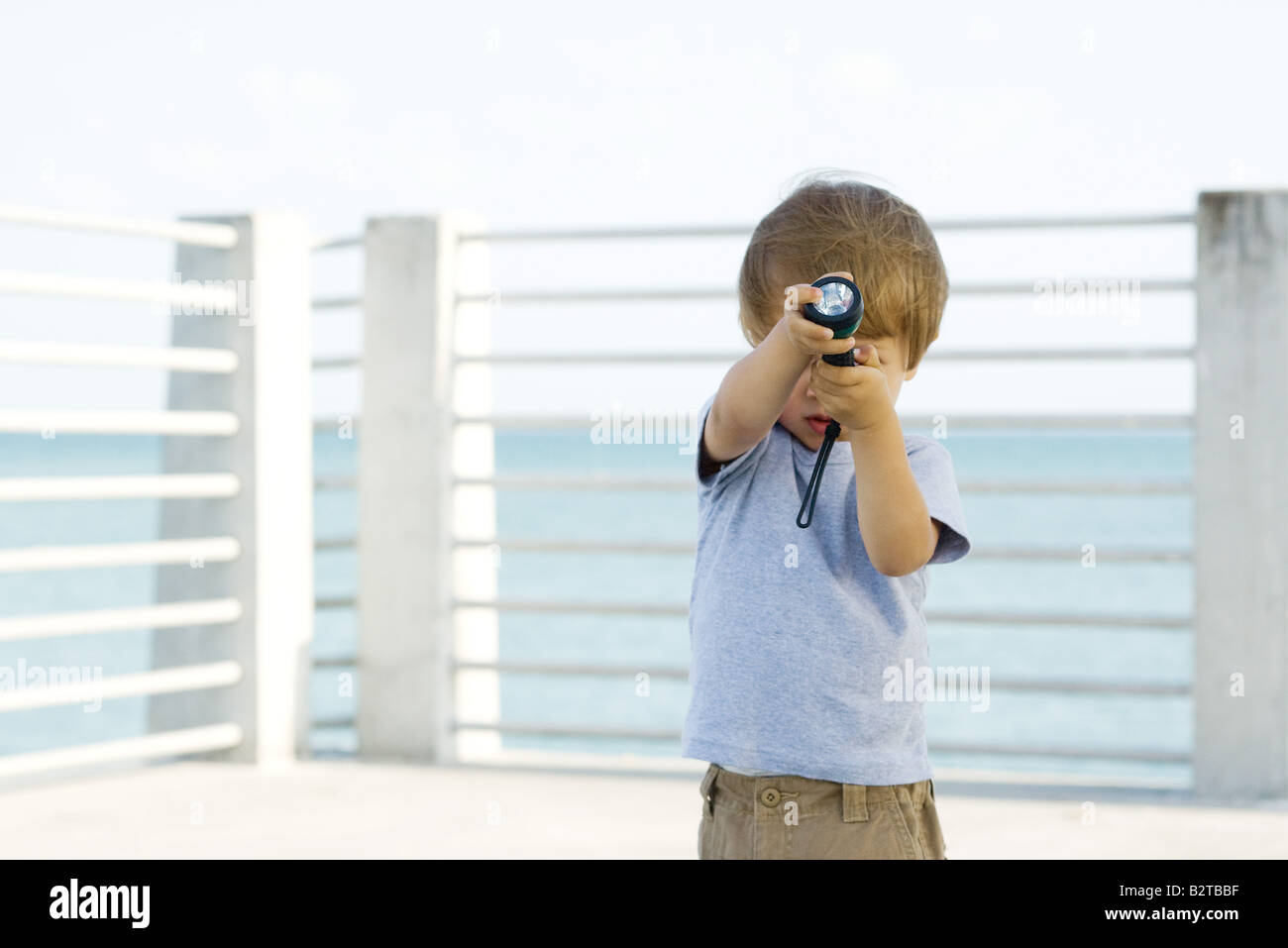 Little boy standing outdoors, holding a flashlight in front of his face ...