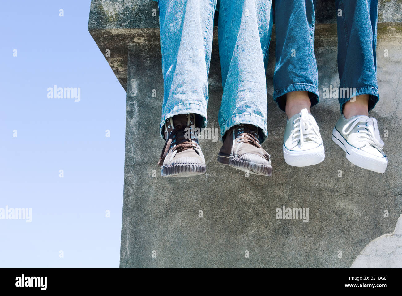 Two pairs of legs dangling over concrete ledge Stock Photo - Alamy