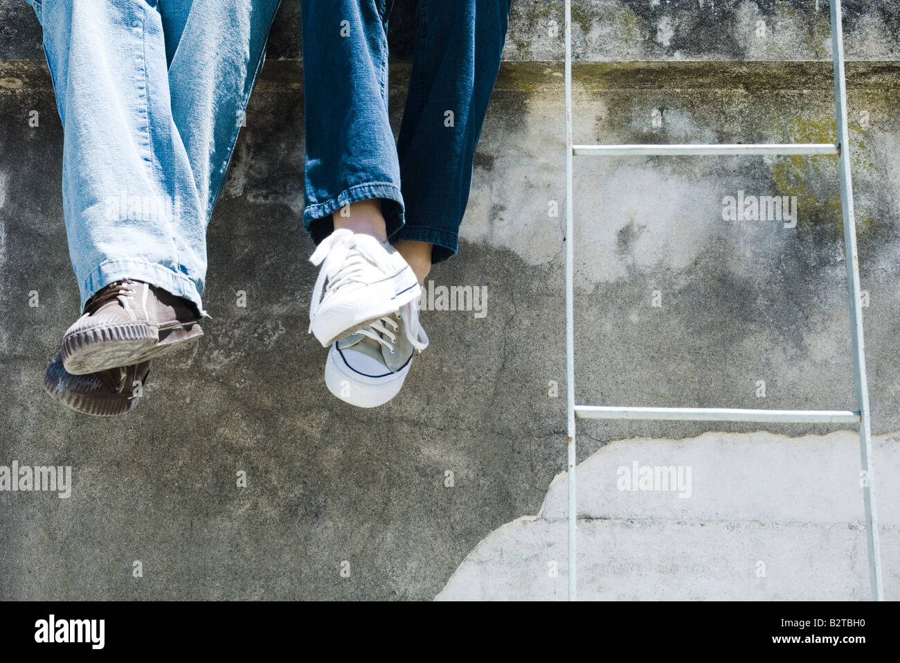 Two people sitting beside ladder, legs crossed at ankle, cropped view ...