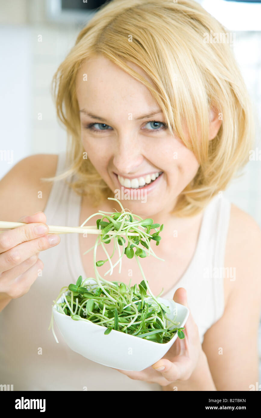 Woman eating radish sprouts with chopsticks, smiling at camera Stock ...