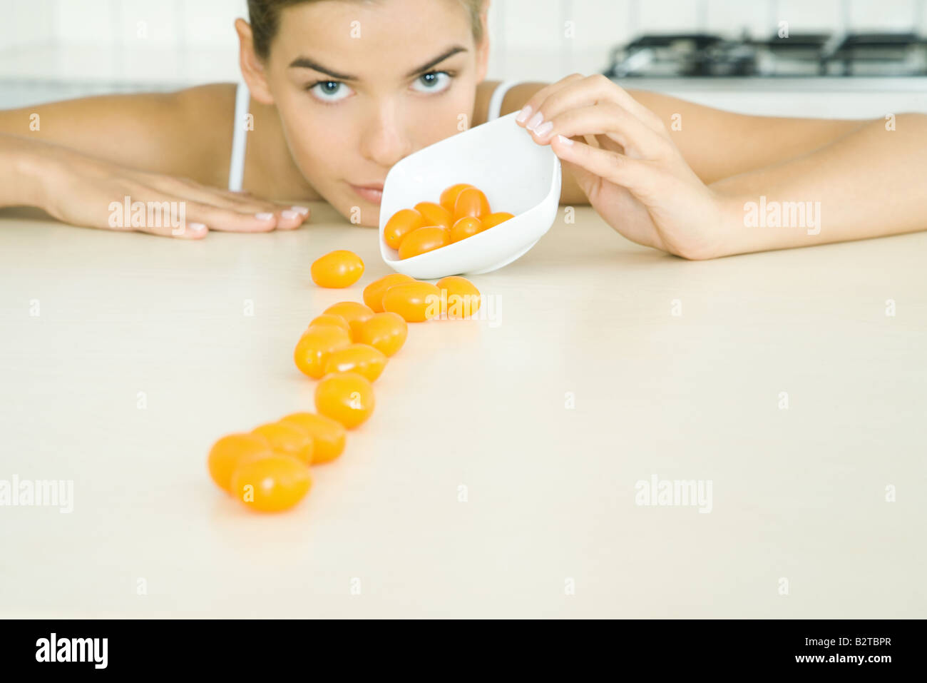 Woman spilling yellow cherry tomatoes out of a small dish, looking at ...