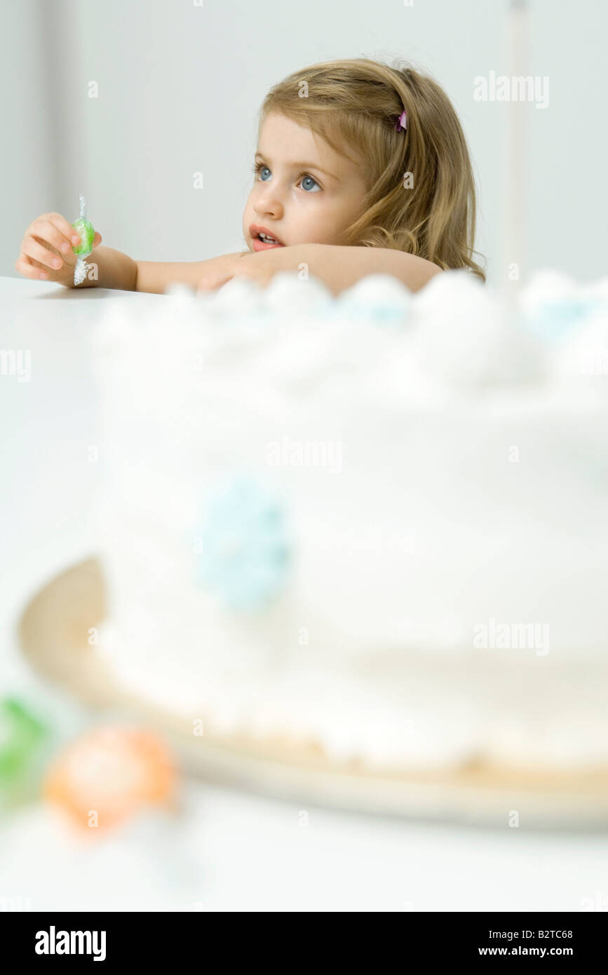Little girl holding candy, birthday cake in foreground Stock Photo - Alamy