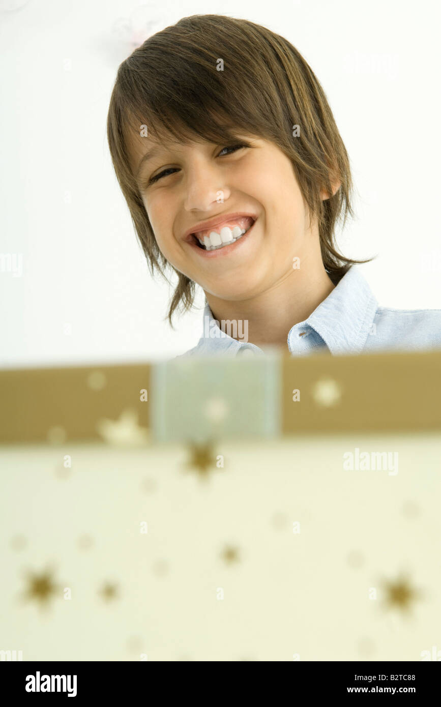 Boy looking over wrapped box, smiling at camera, focus on background ...