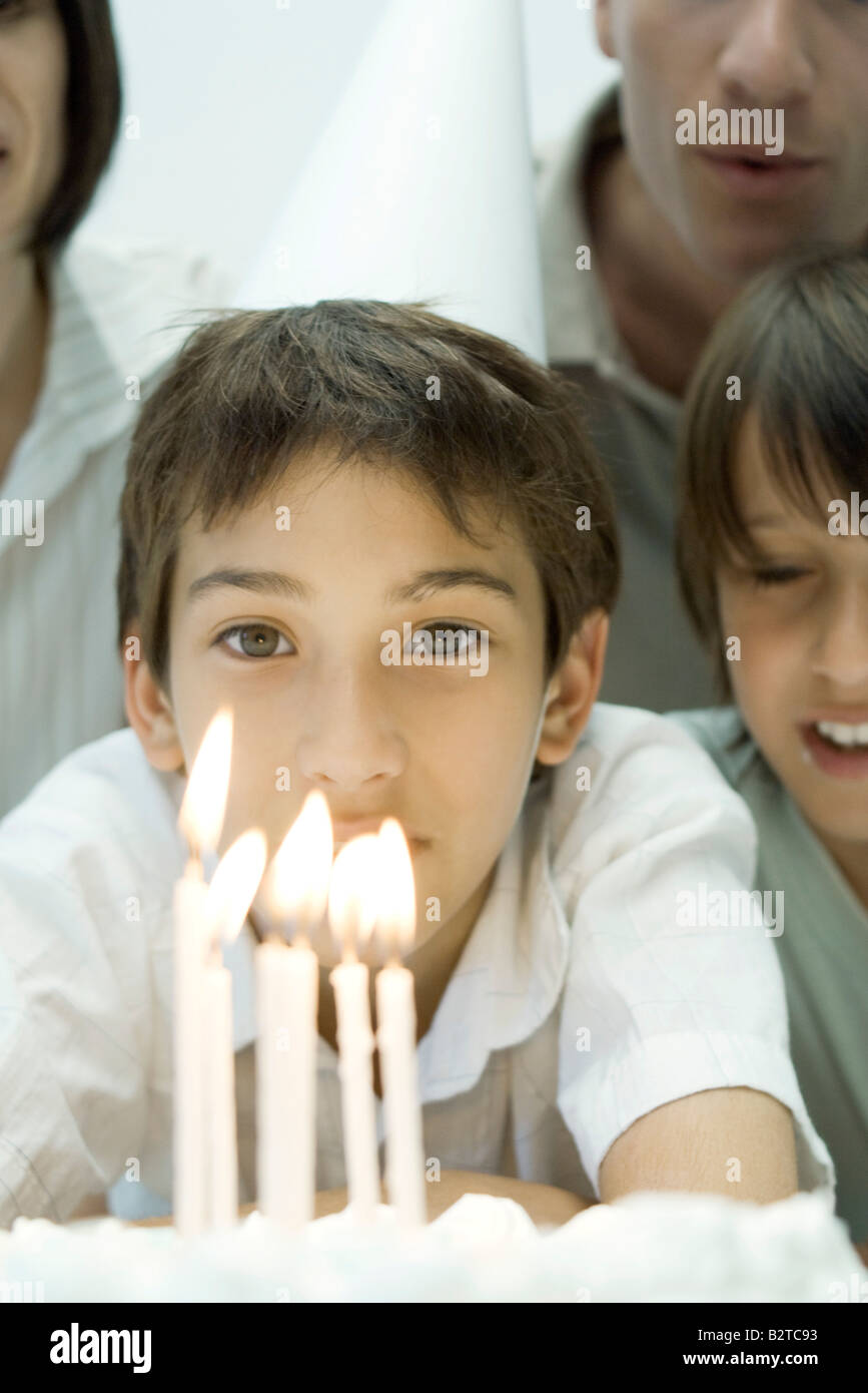 Boy behind birthday cake with lit candles, wearing party hat ...