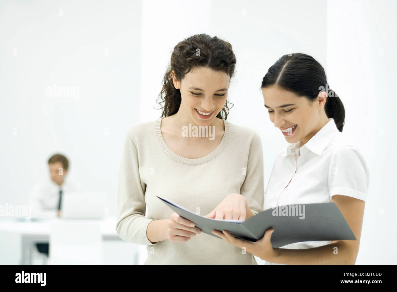 Female colleagues looking at document together, smiling Stock Photo - Alamy