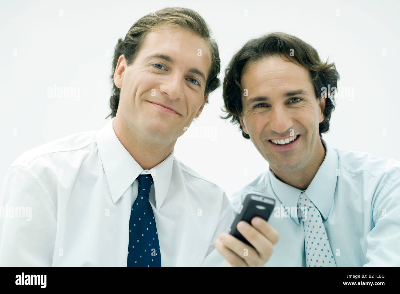 Business partners side by side, smiling at camera, one holding cell ...