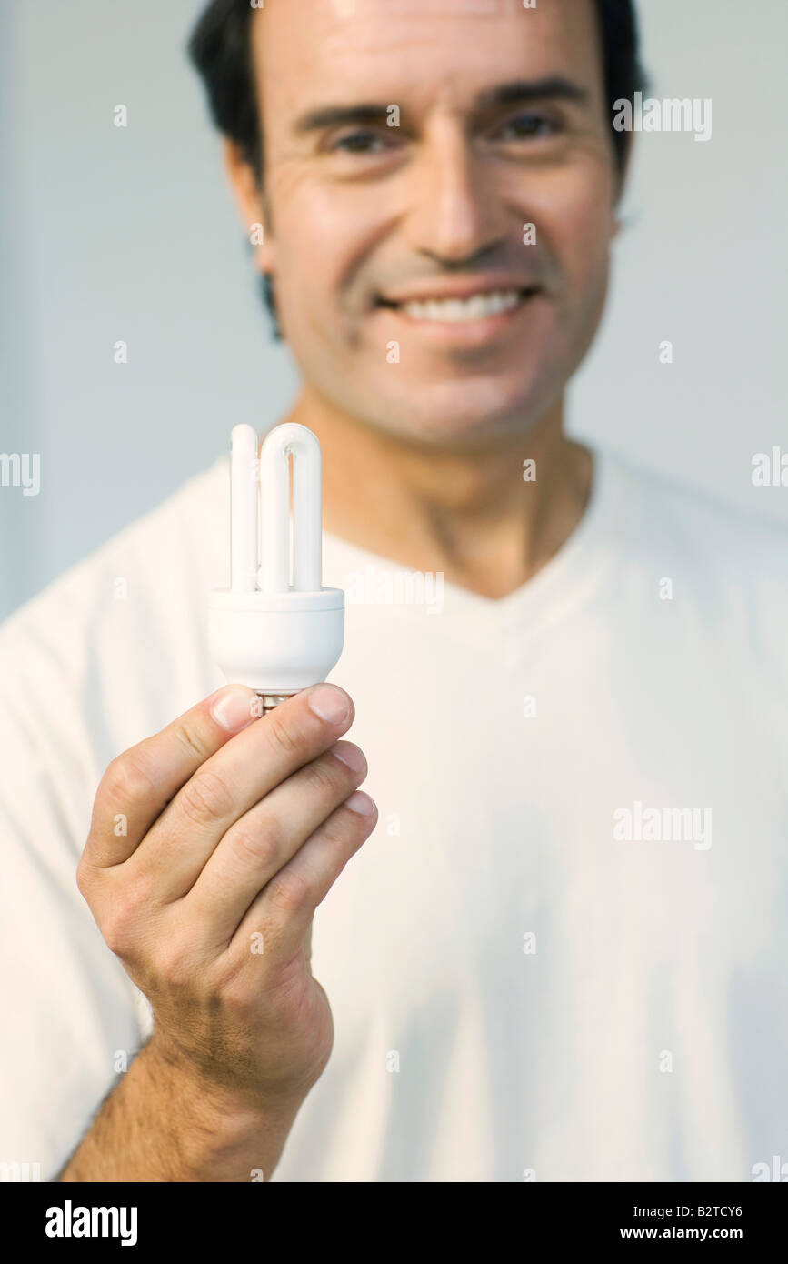Man holding energy efficient light bulb, smiling at camera Stock Photo ...