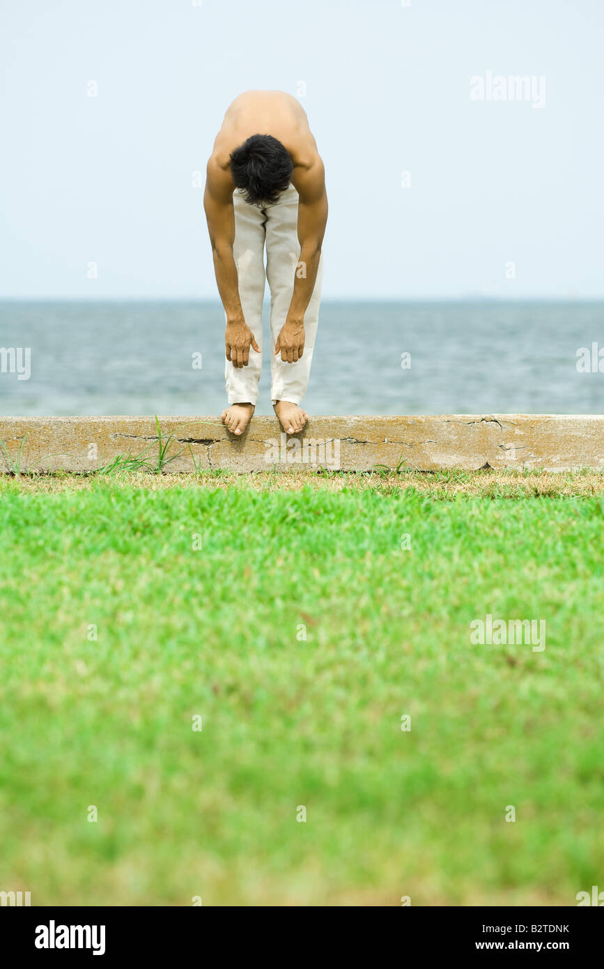 Man standing on low wall outdoors, bending over Stock Photo - Alamy