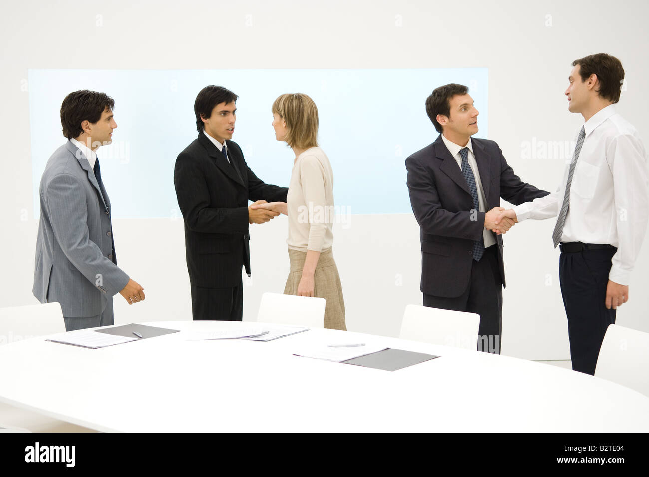 Group of professionals standing beside table, smiling, some shaking ...