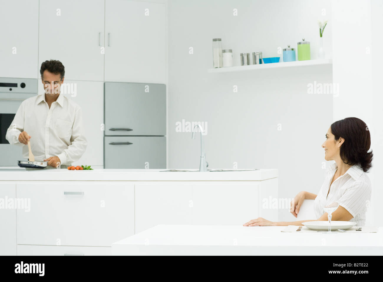 Woman sitting at table looking back over shoulder, husband preparing ...