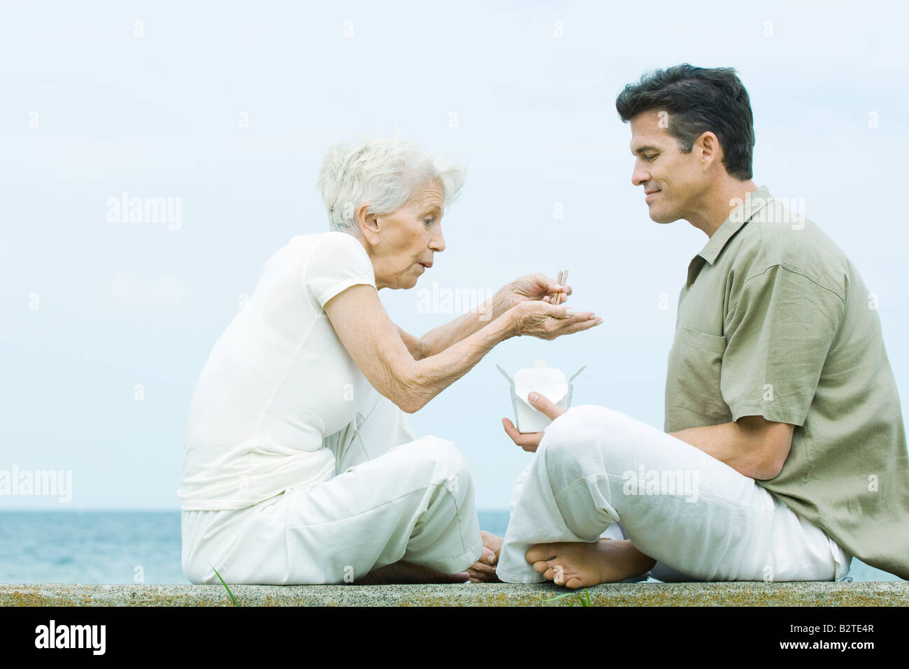 Senior woman and adult son sitting face to face, sharing take out food ...