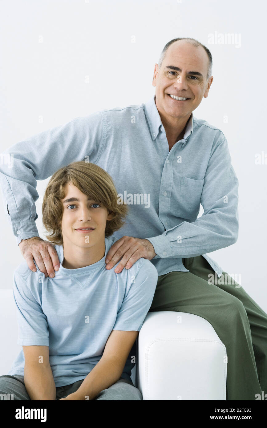 Father and son sitting on sofa, man's hands on teen boy's shoulders ...