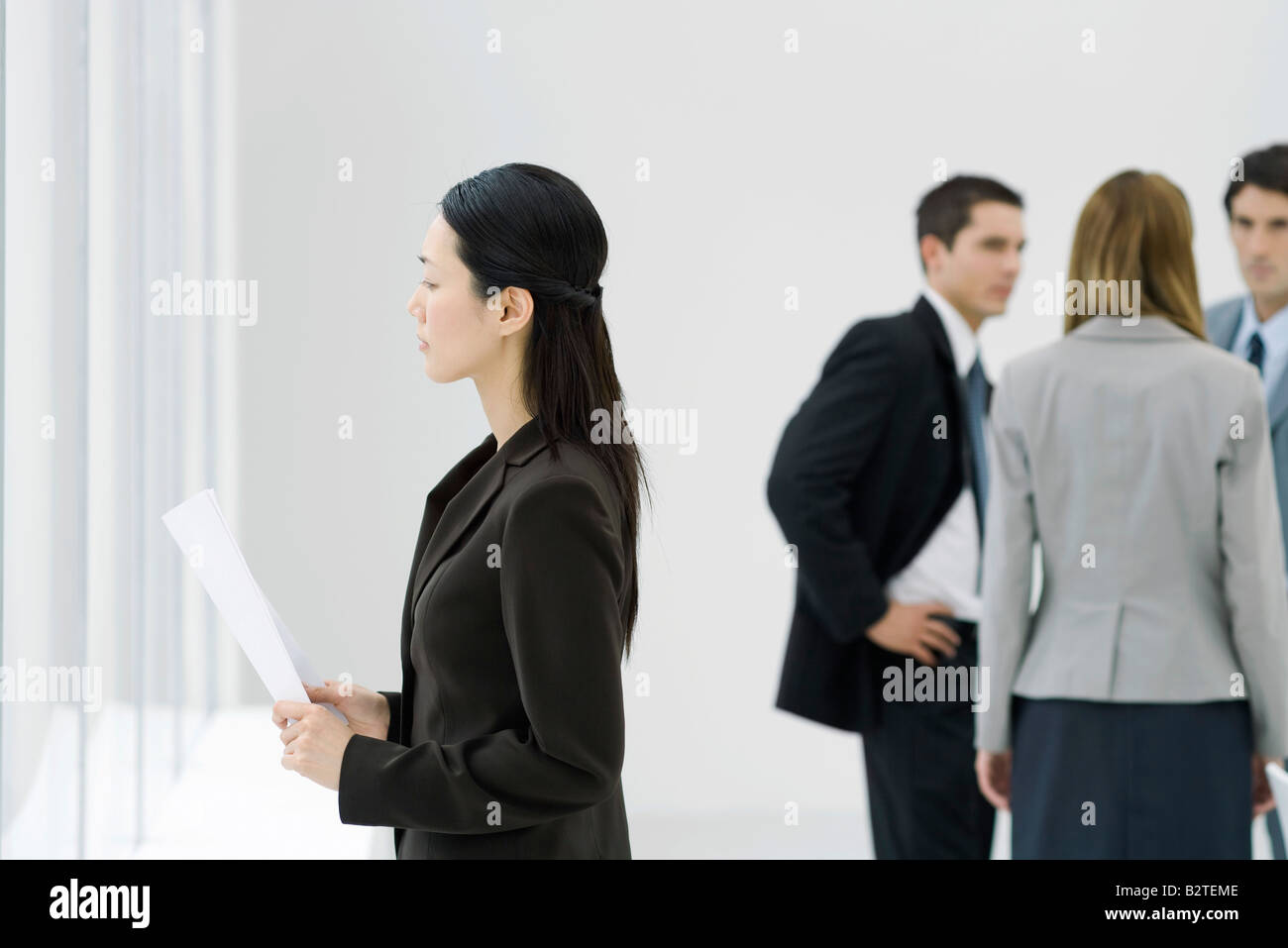 Businesswoman looking out window, holding document, colleagues talking ...