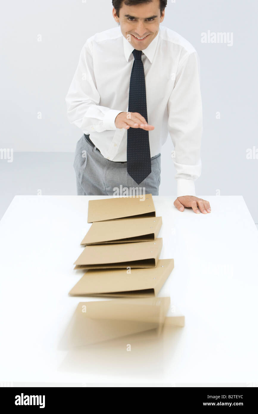 Businessman knocking over binders, smiling at camera Stock Photo - Alamy