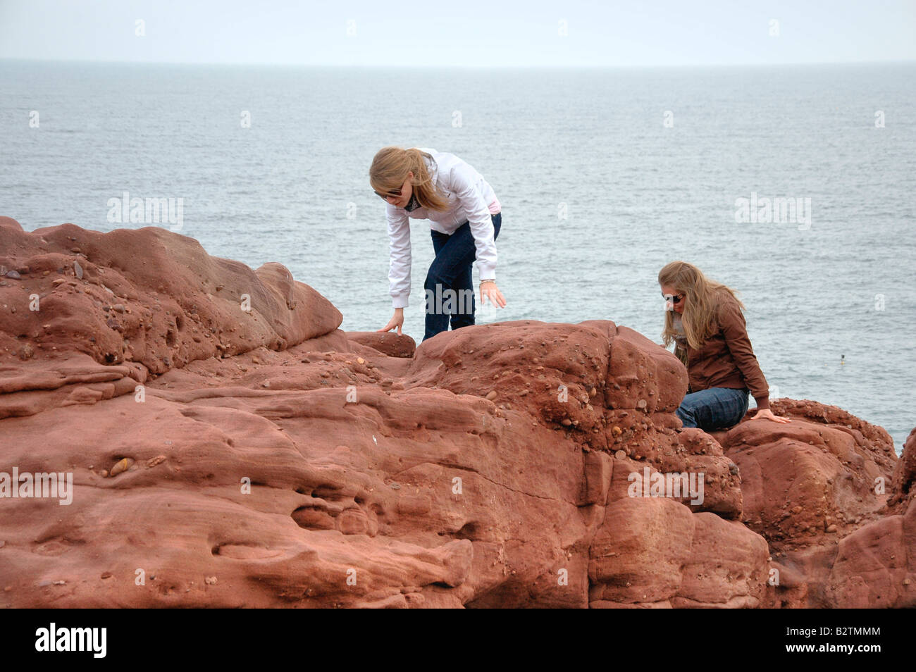 Two young woman clamber over cliff rocks Stock Photo - Alamy