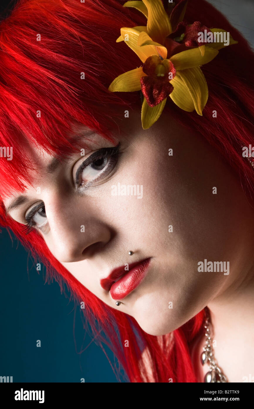Headshot portrait of a young goth girl with bright red hairr on a blue ...