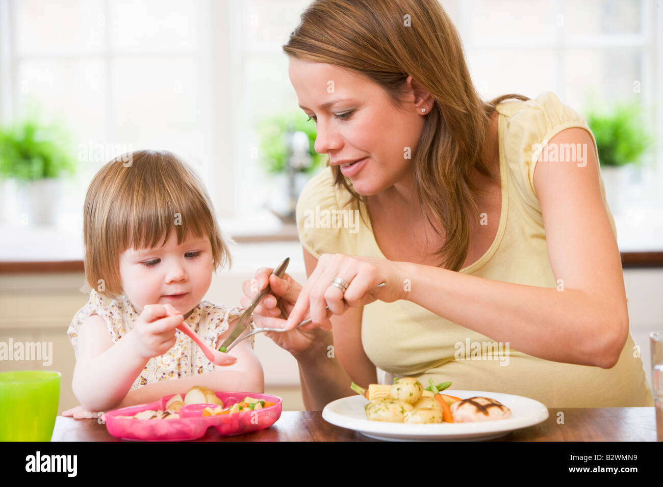 Pregnant mother in kitchen eating chicken and vegetables helping ...