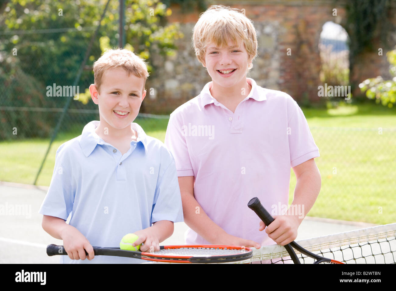 Two young male friends with rackets on tennis court smiling Stock Photo ...