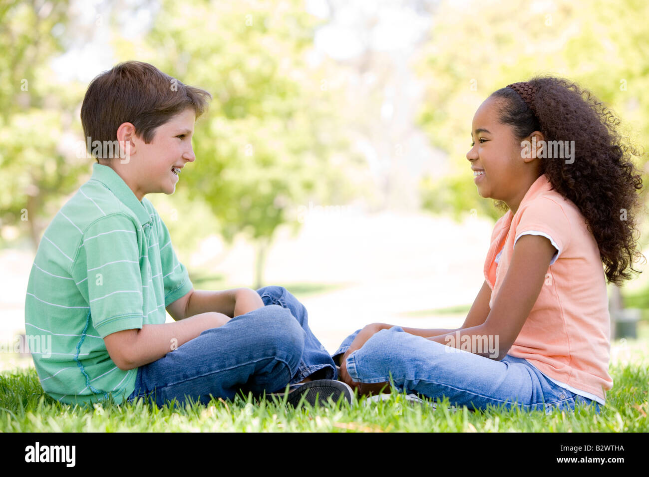 Tow young friends sitting outdoors looking at each other and smiling ...