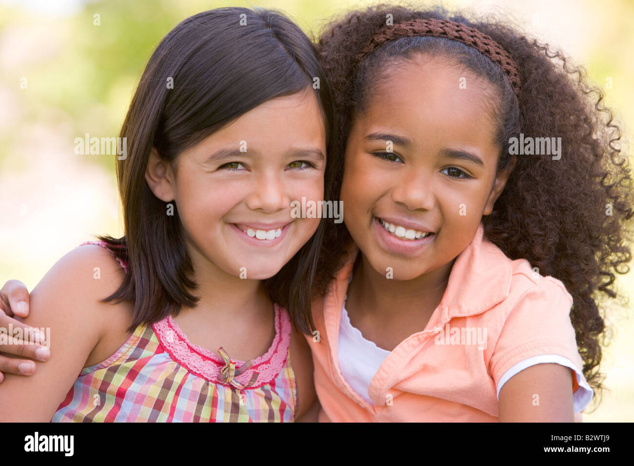 Two young girl friends sitting outdoors smiling Stock Photo - Alamy