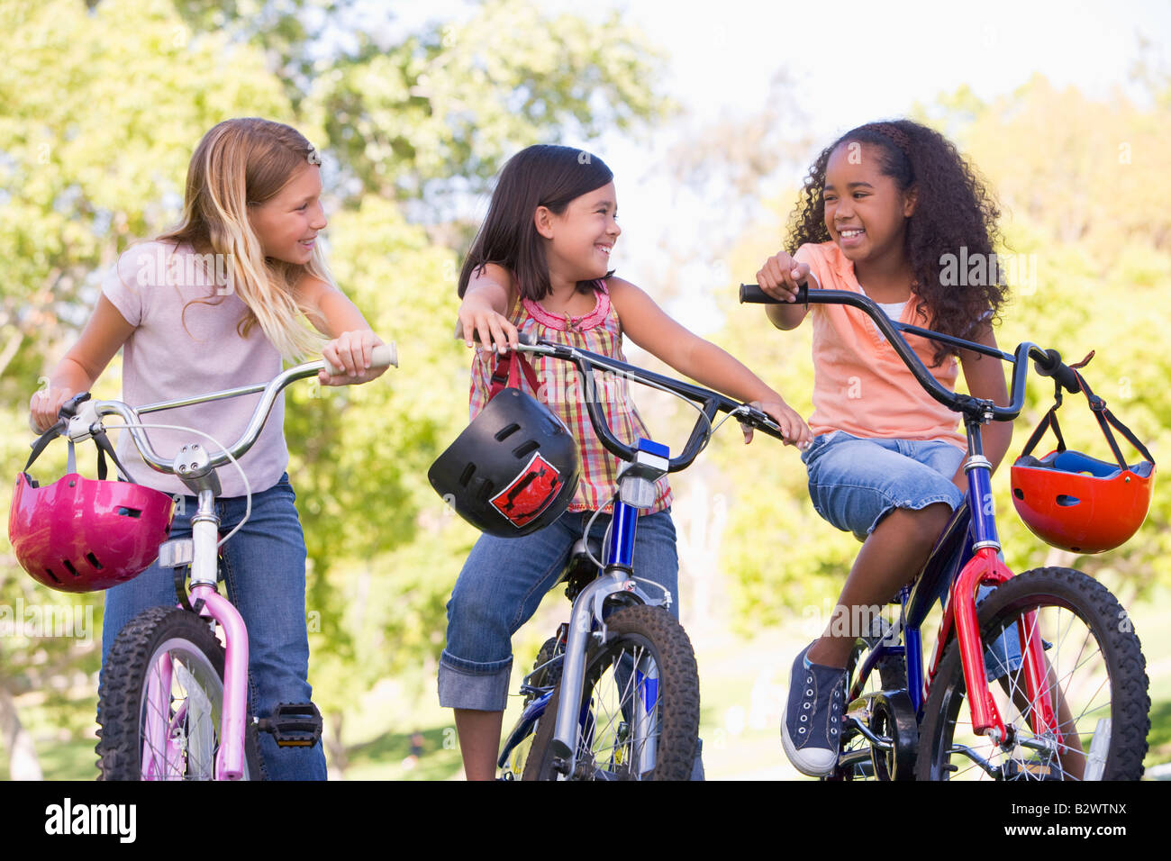 Three young girl friends outdoors on bicycles smiling Stock Photo - Alamy