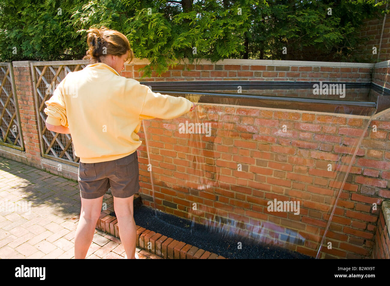 Woman placing finger into garden water fountain Stock Photo - Alamy