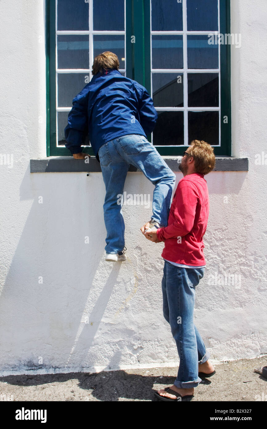 A friend boosts his friend up to get a better view through a window ...