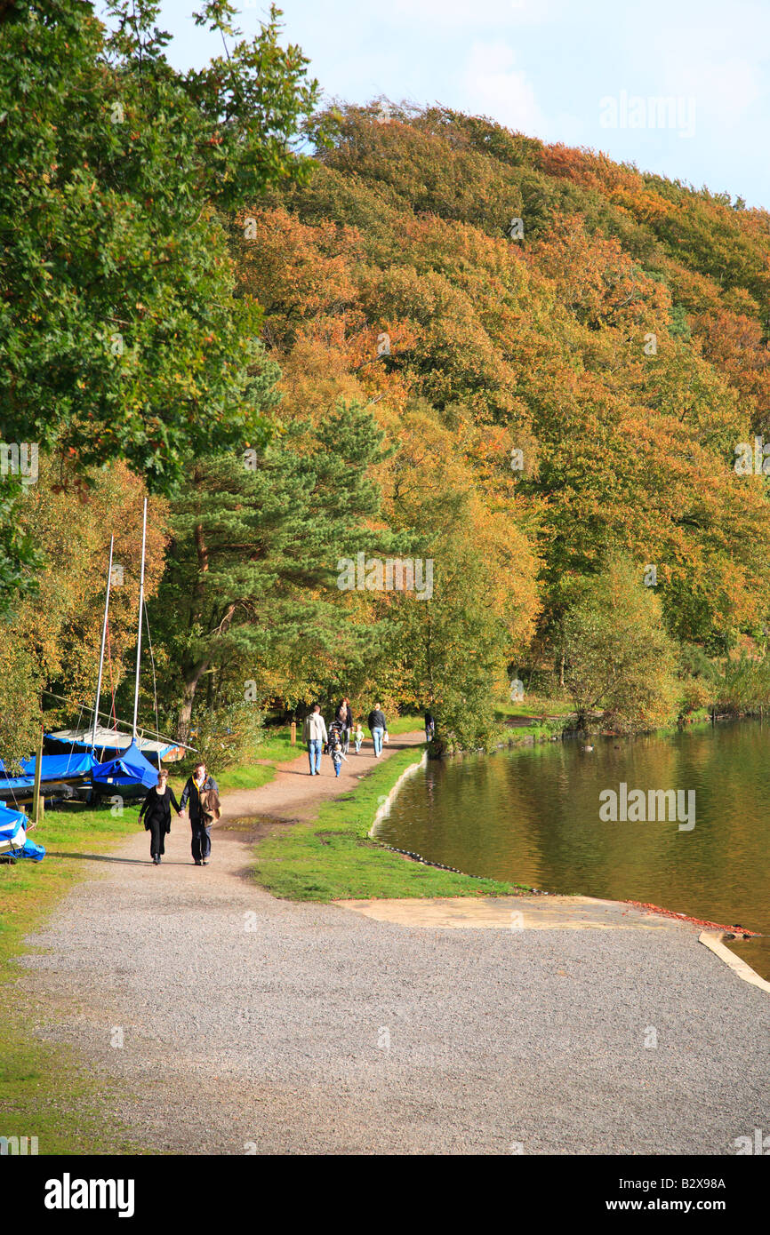 Couple walking along a path by a lake with trees in Autumn colours ...