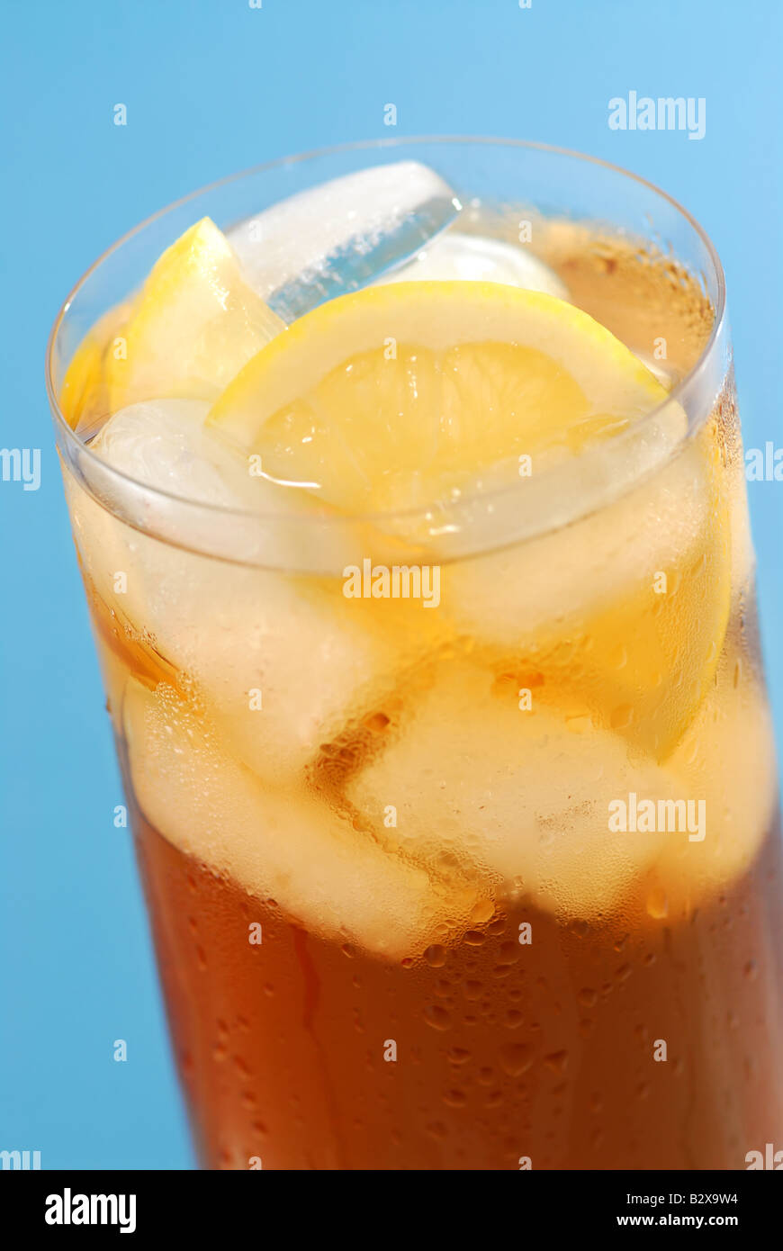 Glass of cold lemon iced tea with ice and lemon on blue background ...