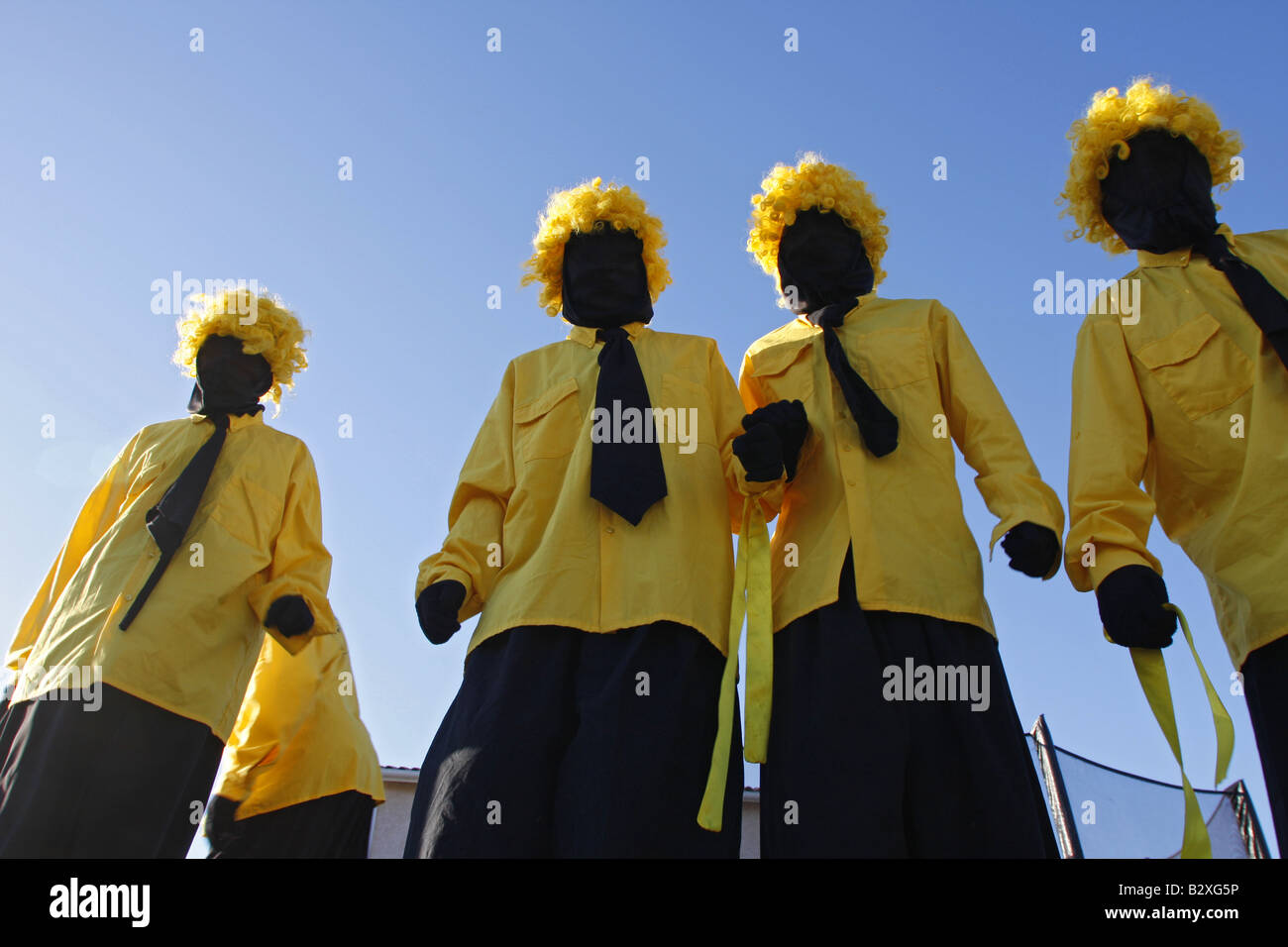 Group of young people in yellow costumes walking on stilts, blue sky ...