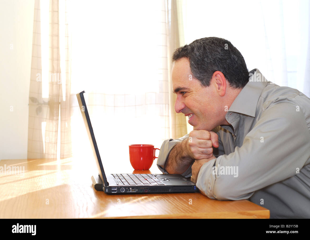 Man sitting at his desk with a laptop looking happy Stock Photo - Alamy