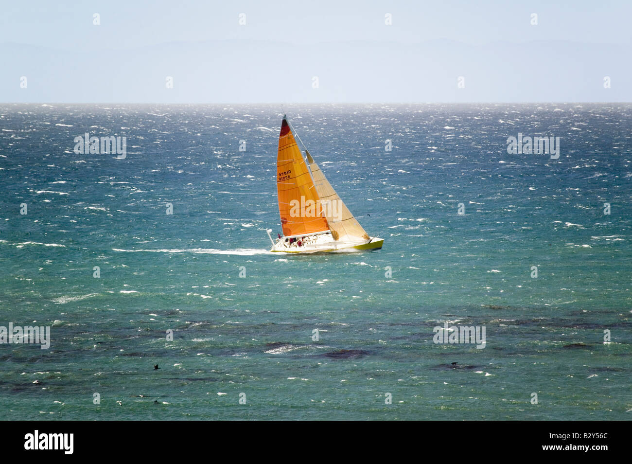 A sailboat with a bright orange sail gliding across the Pacific Ocean ...