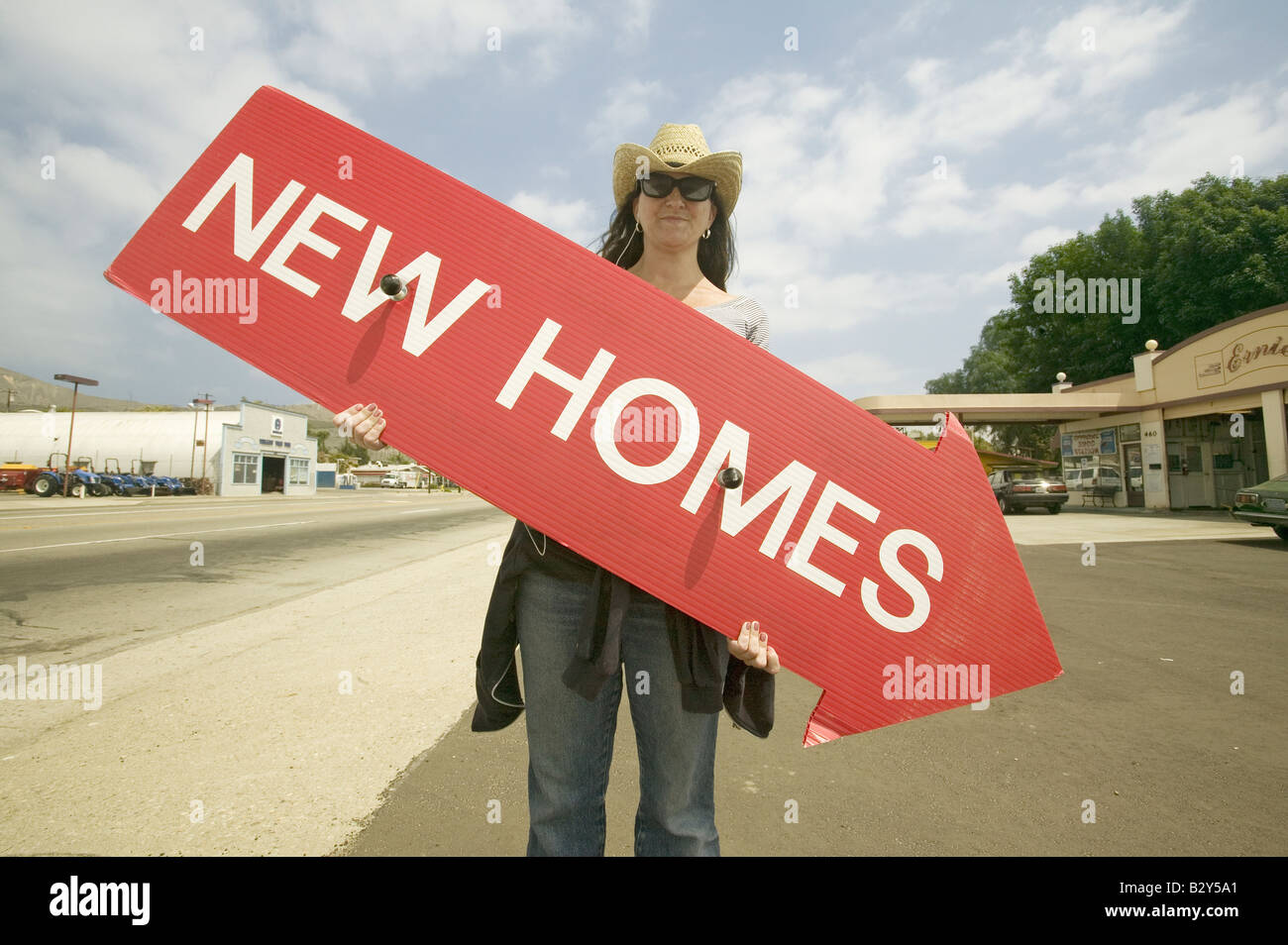 Girl holding red sign with arrow pointing down, that reads "New Homes ...