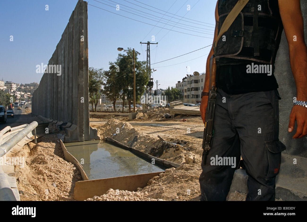 Armed guard with weapon guarding the Israeli West Bank barrier, cropped ...