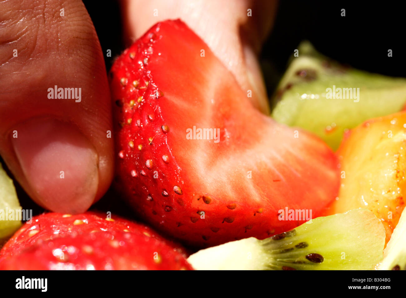 Human Fingers picking up a Red Strawberry from Freshly Cut Mixed Fruit ...