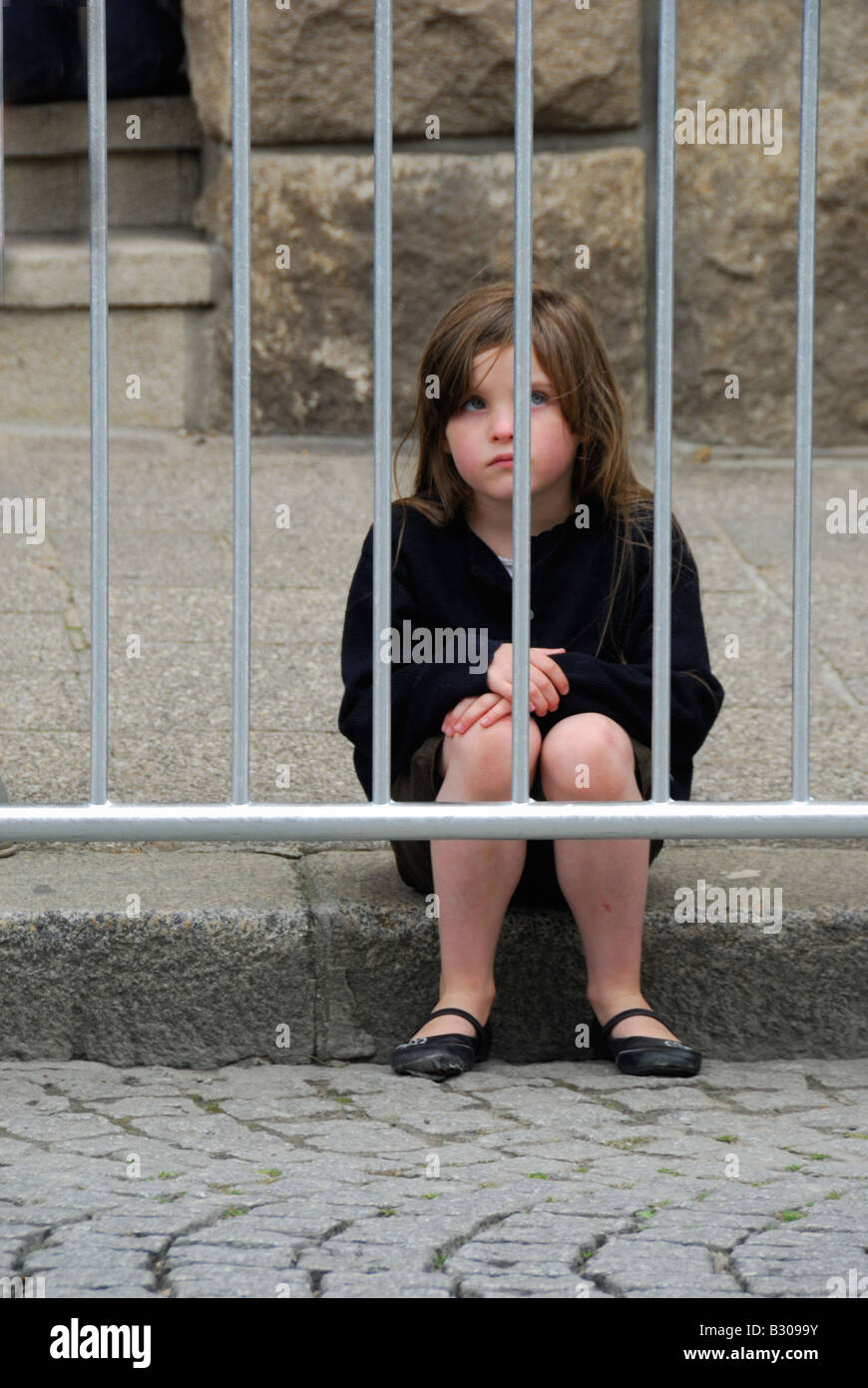Young girl sitting on the pavement behind railings Stock Photo - Alamy