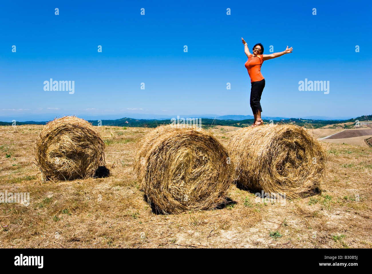 Middle aged woman depicting freedom by standing on rolls of hay in farm ...