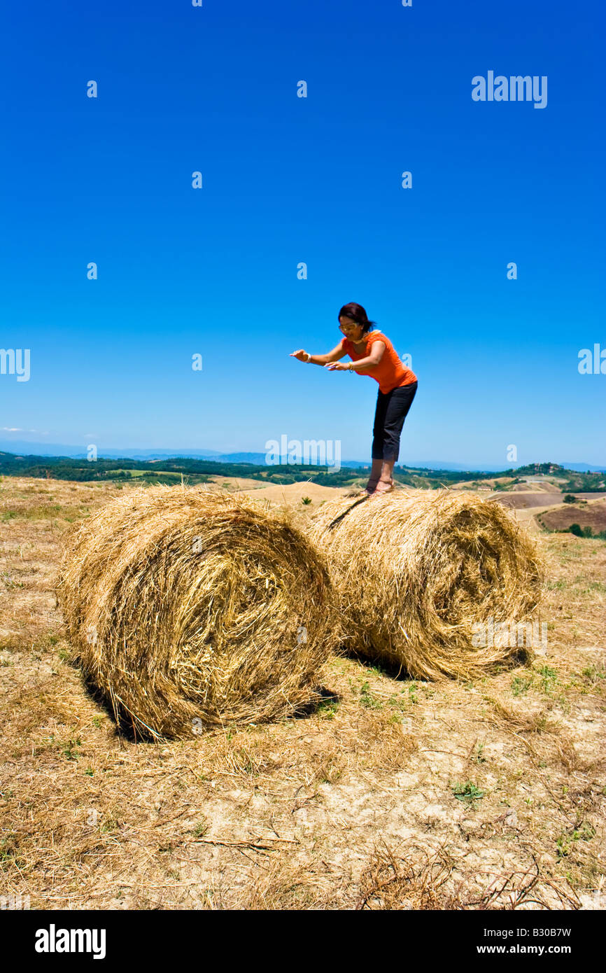 Middle aged woman depicting freedom by standing on rolls of hay in farm ...