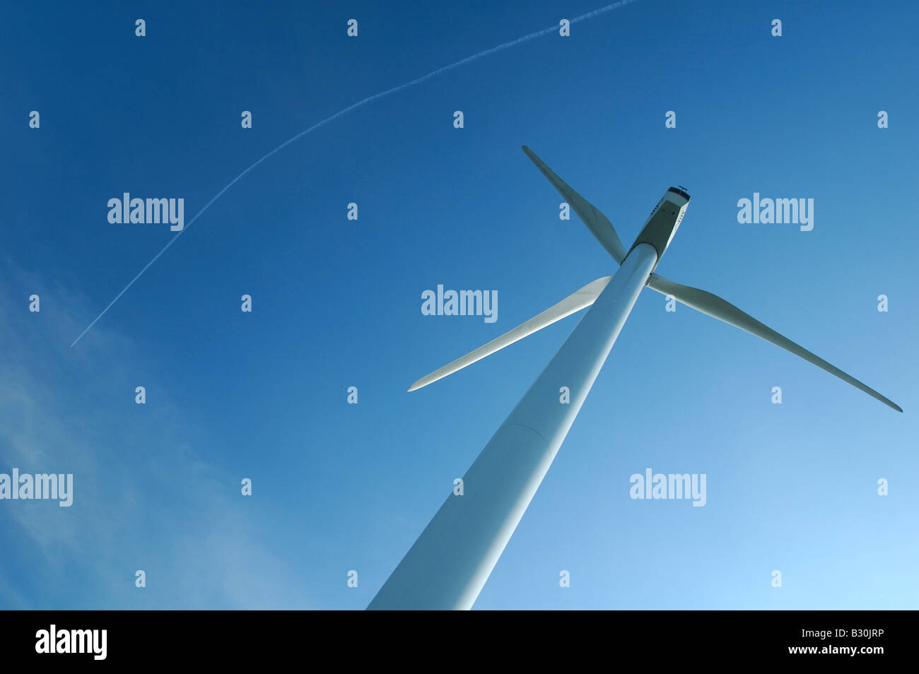 Wind turbine with a smoke trace of airliner jet plane on blue sky ...