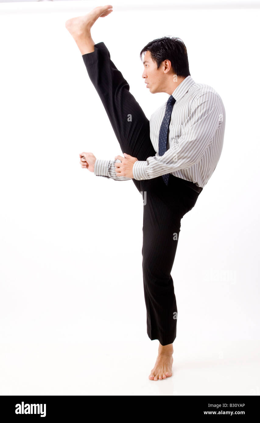A young asian businessman in corporate dress does a high karate kick ...