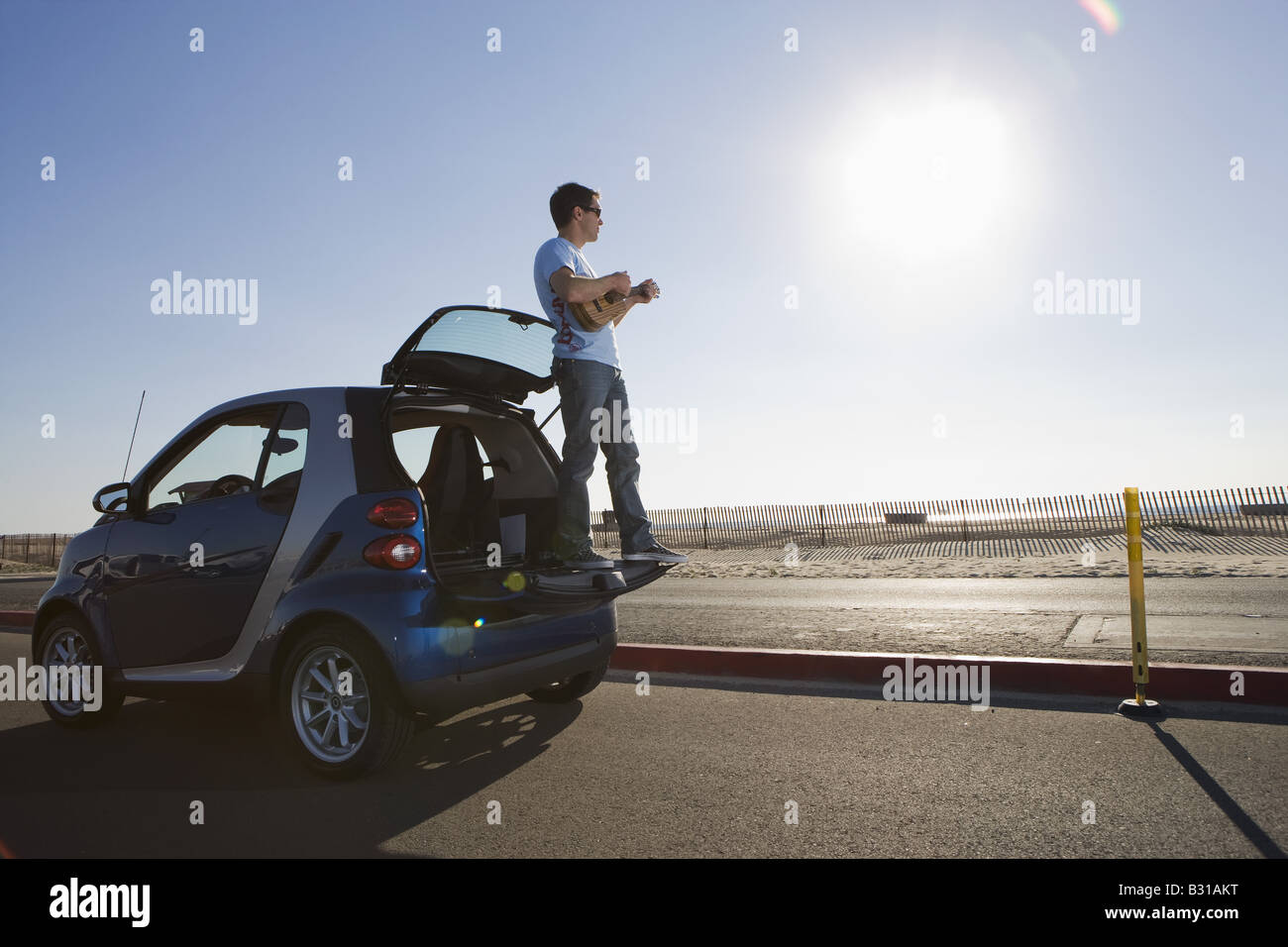 Young man standing on rear of Smartcar at beach Stock Photo - Alamy