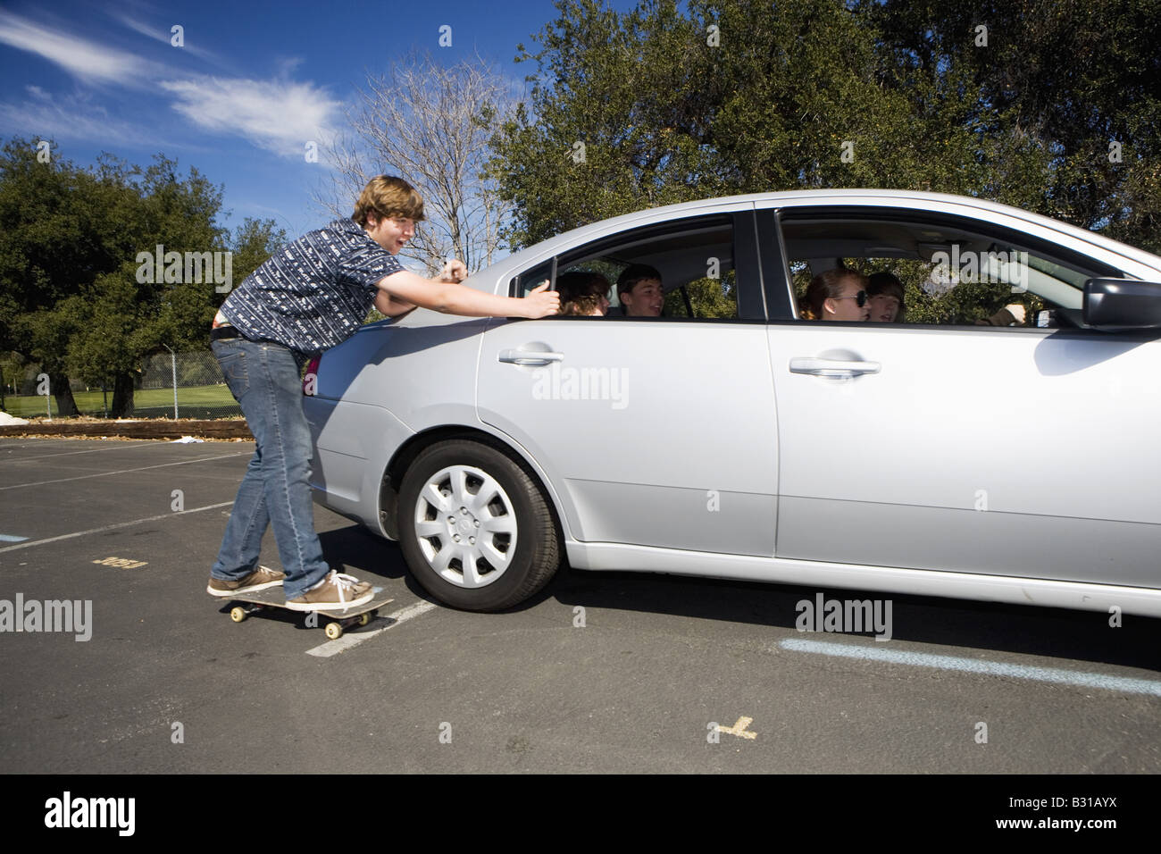Teens in car pulling along friend on skateboard Stock Photo - Alamy
