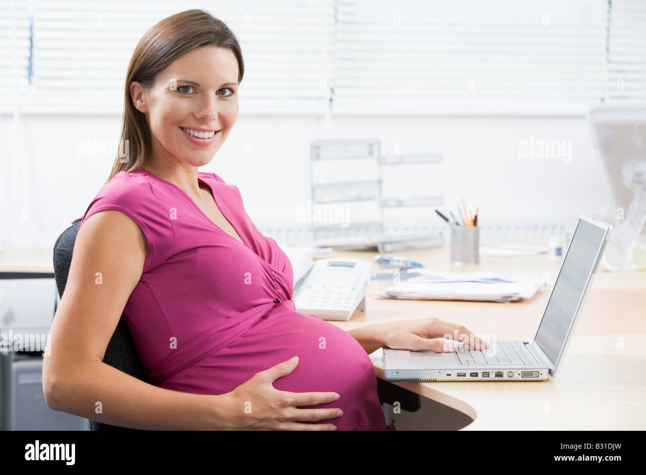 Pregnant woman at work using laptop and smiling Stock Photo - Alamy