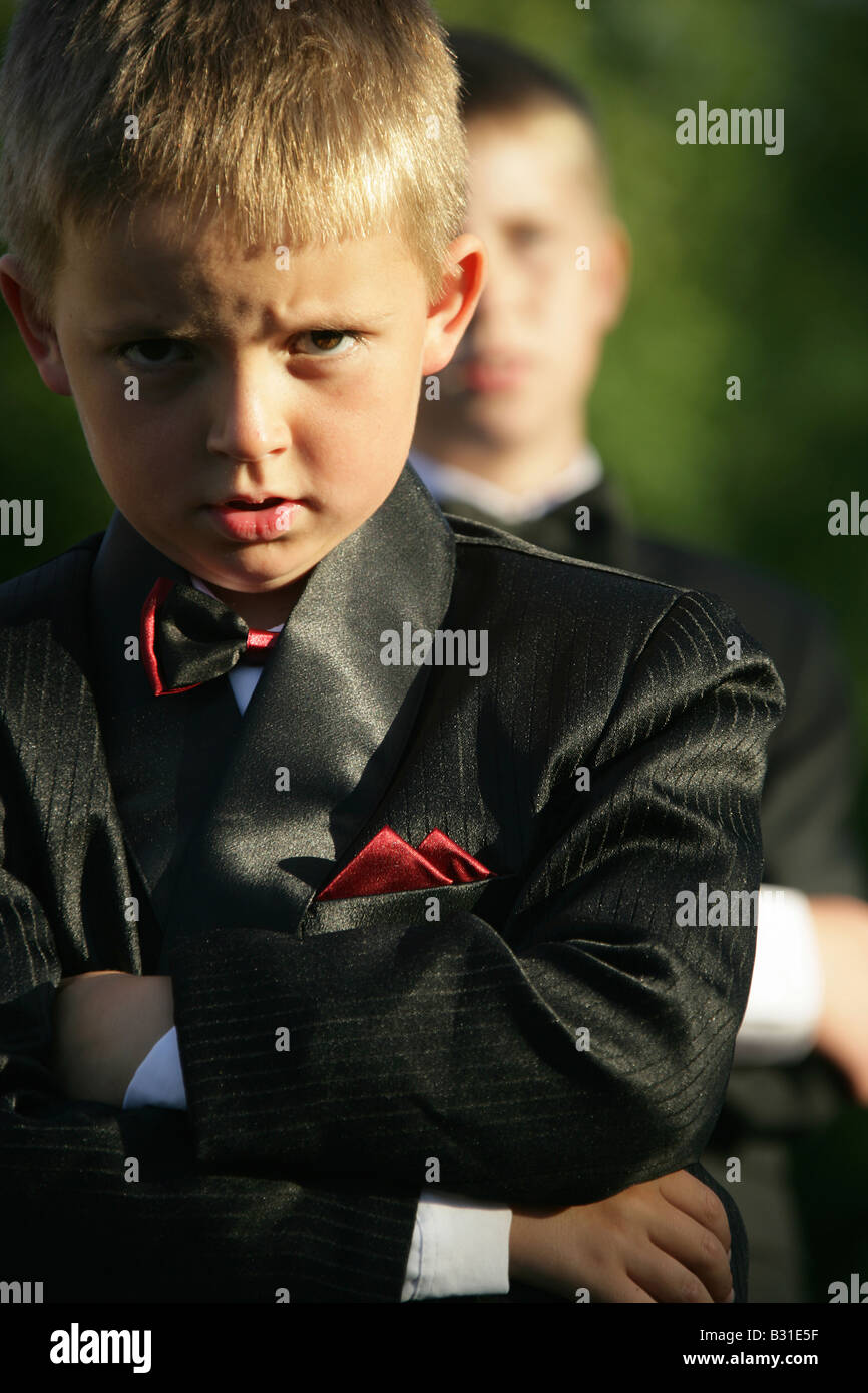 Young boy dressed in a dinner suit with his arms folded and bearing a ...